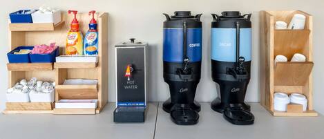 Uma estação de café com duas máquinas de café, um dispensador de água quente e espaço para cápsulas de café e leite.