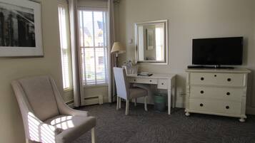 Quarto de hotel com escrivaninha, cadeira, televisão, cômoda e um quadro pendurado na parede.