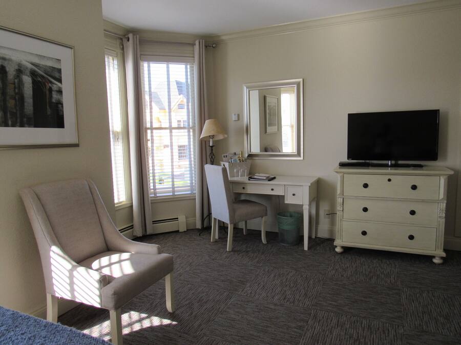 Quarto de hotel com escrivaninha, cadeira, televisão, cômoda e um quadro pendurado na parede.
