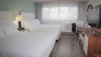 Quarto de hotel com duas camas, uma escrivaninha com televisão, uma cadeira e uma janela com cortinas.