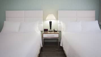 Quarto de hotel com duas camas, mesa de cabeceira com lâmpada, relógio e telefone.