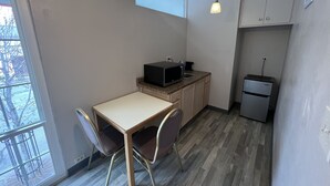 Cozinha compacta com micro-ondas, geladeira e pequena mesa de jantar com cadeiras.