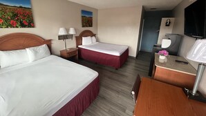 Quarto de hotel com duas camas, uma escrivaninha, uma cadeira, televisão e obras de arte nas paredes.