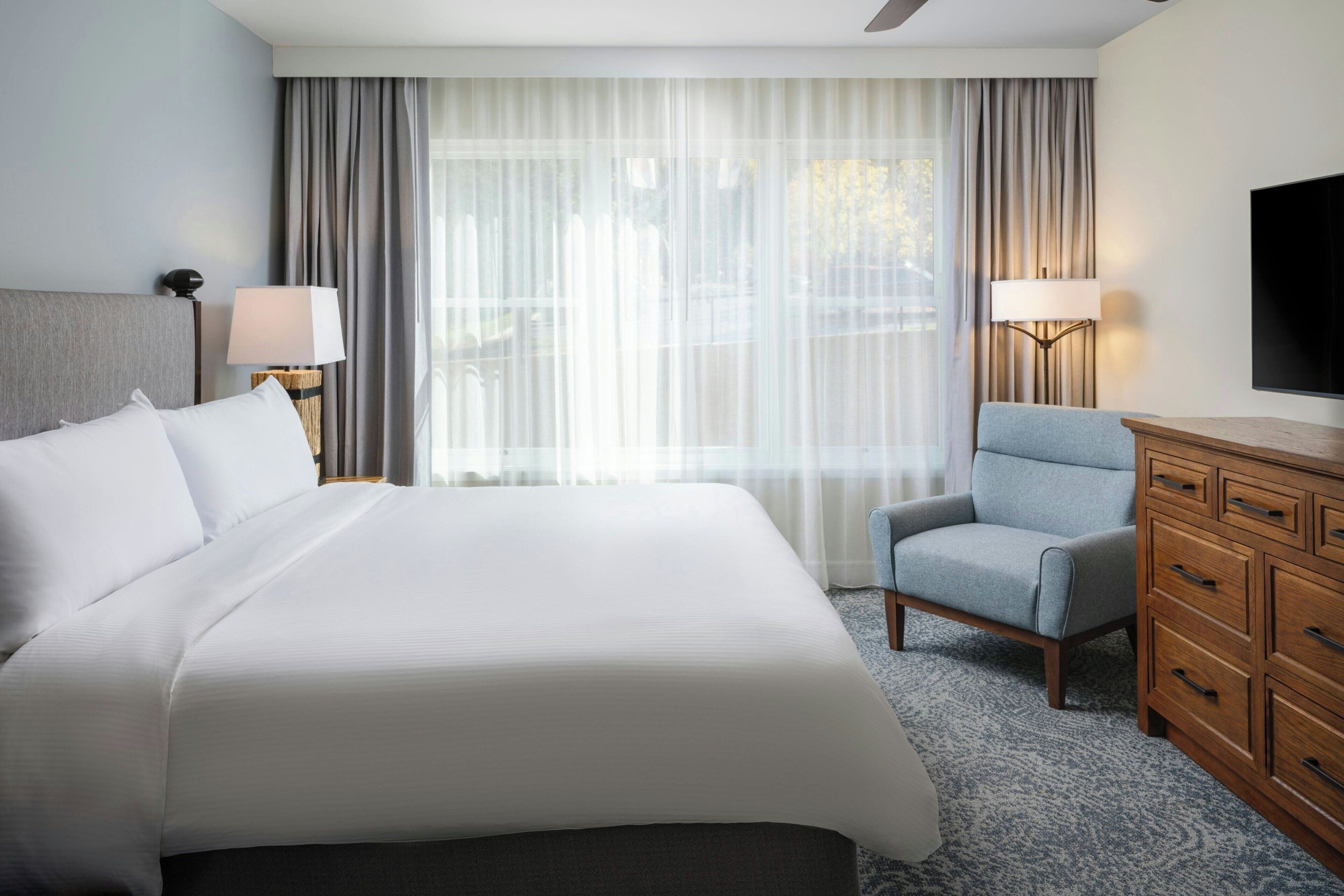 Quarto de hotel com uma cama grande, uma cadeira, uma televisão e uma escrivaninha.