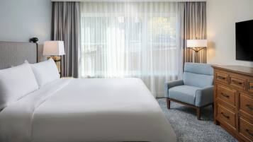 Quarto de hotel com uma cama grande, uma cadeira, uma televisão e uma escrivaninha.