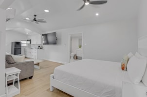 Quarto moderno com cama grande, sofá, televisão e ventoinha no teto.