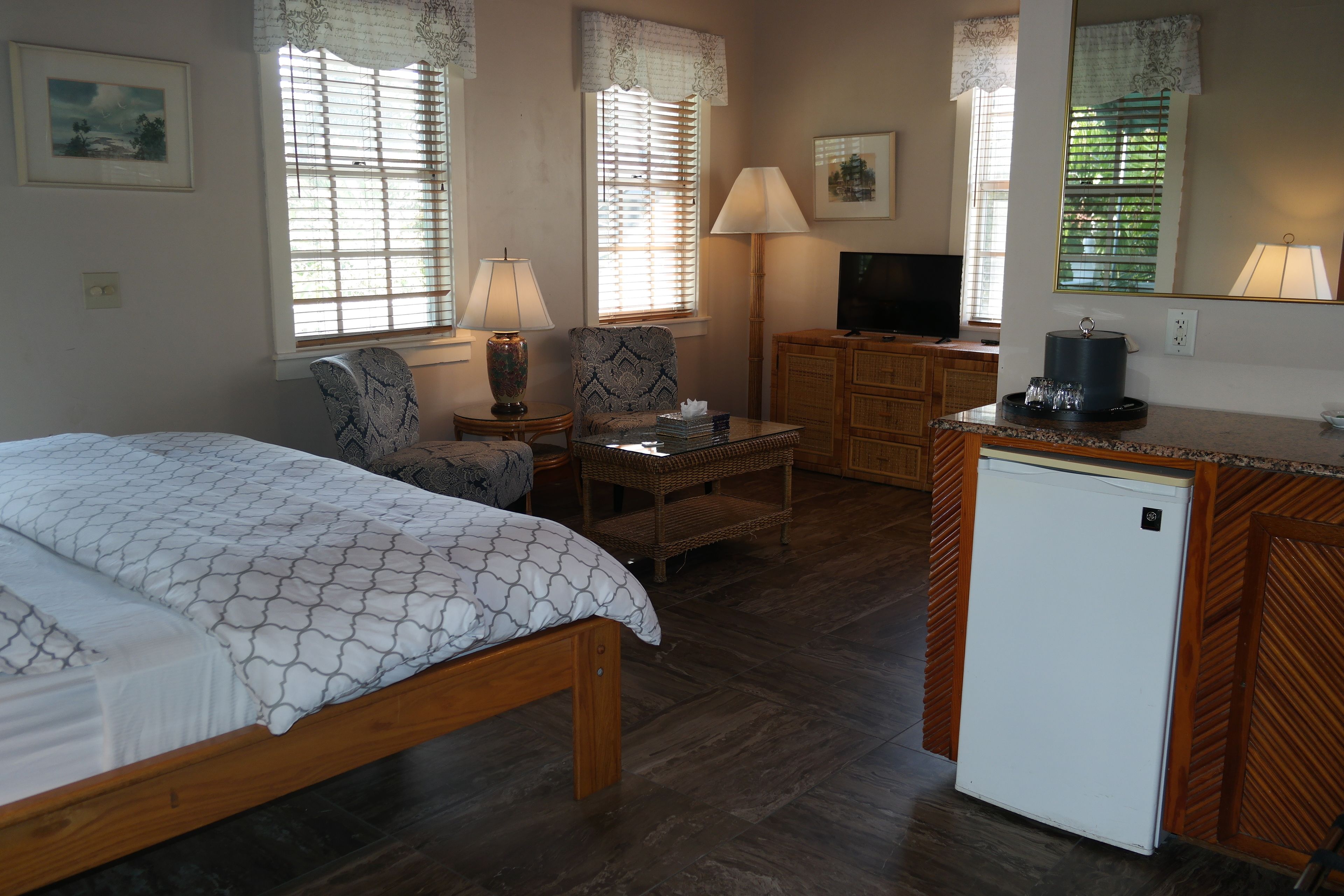 Quarto com cama, cadeira, mesa pequena, televisão e frigorífico.