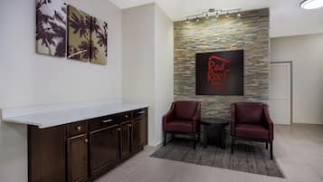 Uma área de recepção com parede de pedra, um letreiro 'Red Roof Inn & Suites', um balcão e duas poltronas.