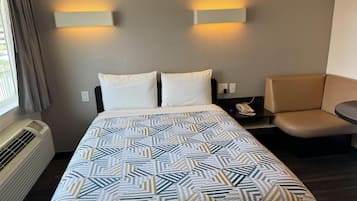 Quarto de hotel com cama, duas luminárias de cabeceira, uma poltrona, telefone e ar condicionado.
