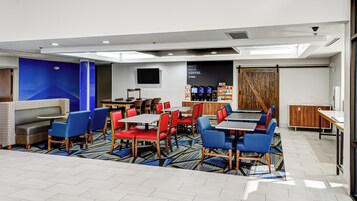 Quarto de hotel com área de refeições, mesas, cadeiras, espaço para café e uma grande janela.