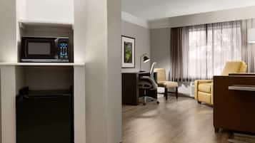 Quarto de hotel com micro-ondas, escrivaninha, cadeira, sofá e uma janela grande com cortinas.