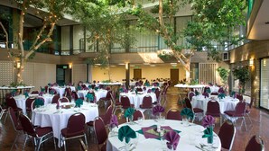 Uma ampla sala de banquetes coberta, com mesas redondas dispostas para refeições, rodeada de cadeiras e decorada com luzes de Natal.