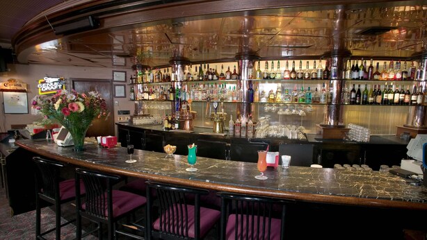 Uma área de bar com bancada de mármore, vários bancos altos e diversas garrafas e copos em prateleiras.