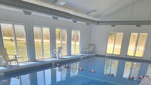 Piscina interna com água azul cristalina, prancha de salto e cadeira do salva-vidas.