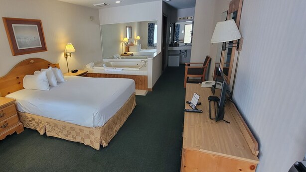 Quarto de hotel com uma cama grande, mesas de cabeceira, uma escrivaninha com cadeira, um espelho e banheiro com banheira e pia.