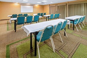 Uma sala de conferências com mesas, cadeiras, piso coberto de carpete e um projetor na parede.