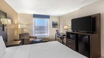 Quarto de hotel com cama grande, escrivaninha, cadeira, televisão e frigorífico.
