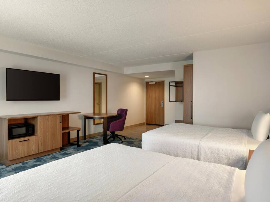 Quarto de hotel com duas camas, uma escrivaninha, uma cadeira, uma televisão de tela plana e um micro-ondas.