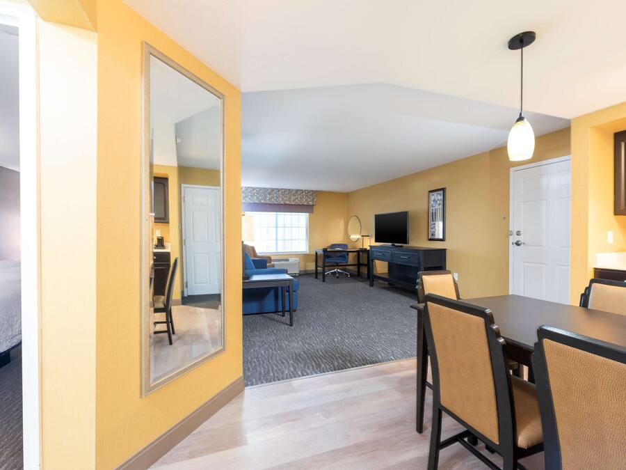 Quarto de hotel com cama, escrivaninha, cadeira, televisão e mesa de jantar com cadeiras.