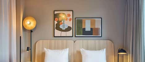 Quarto de hotel com uma cama de casal, duas mesinhas de cabeceira, um abajur e duas obras de arte emolduradas na parede.