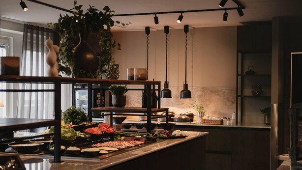 Uma cozinha moderna com uma ilha central exibindo diversos alimentos, luminárias pendentes e um vaso de planta.