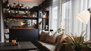 Uma sala de estar acolhedora com um sofá escuro, uma mesa de centro e uma estante com objetos decorativos e livros.