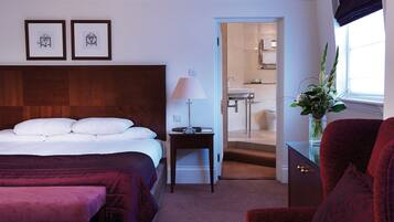 Quarto de hotel com cama, mesa de cabeceira, luminária, cadeira e vista para o banheiro.