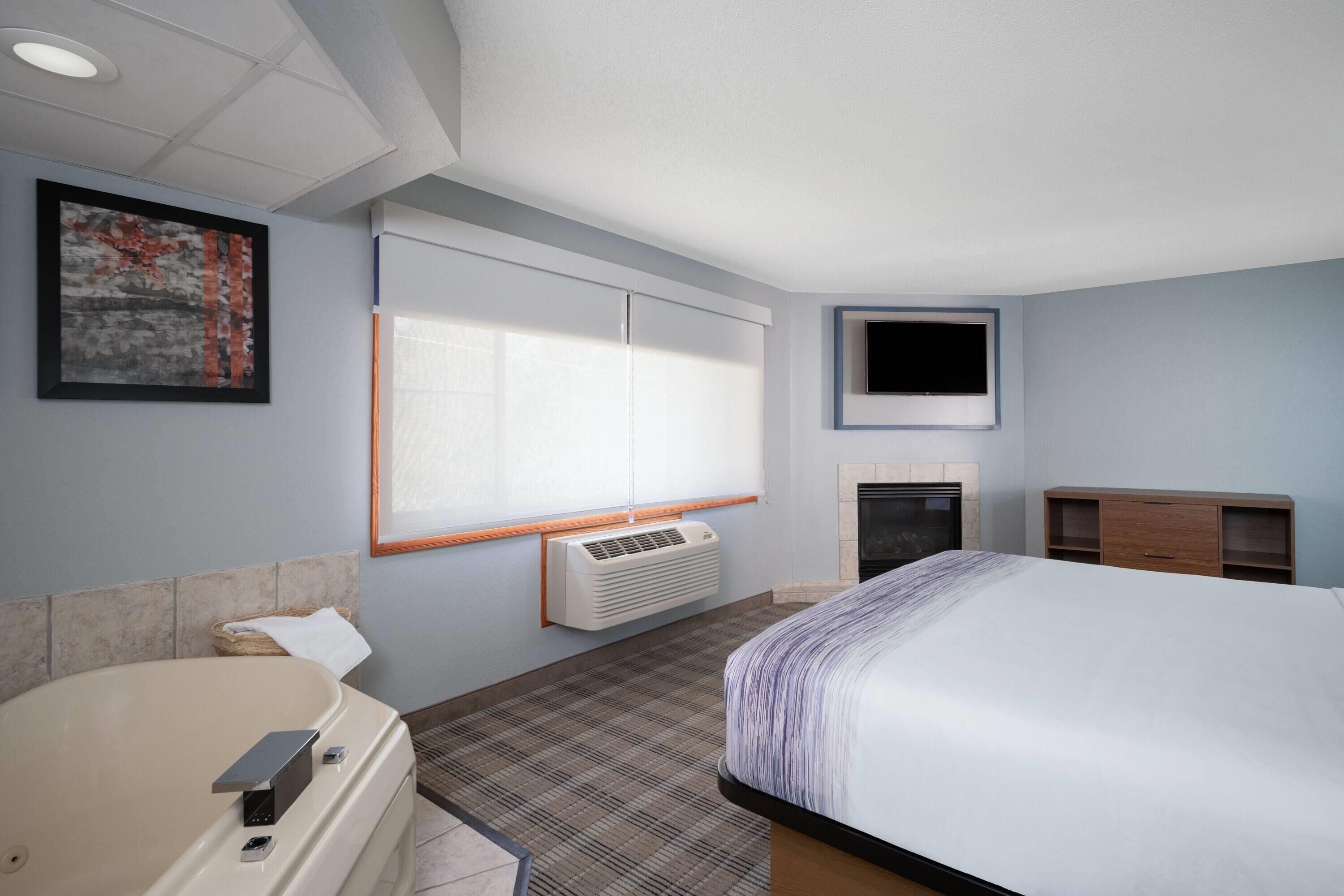 Quarto de hotel com uma cama grande, banheira, lareira e televisão na parede.