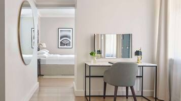 Quarto de hotel moderno com cama, escrivaninha, cadeira, espelho grande e janela com cortinas.