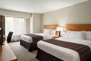 Quarto de hotel com duas camas, uma escrivaninha, uma cadeira e uma televisão.