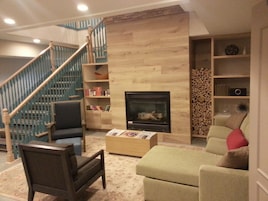Uma sala de estar com lareira, escadas e uma estante de livros.