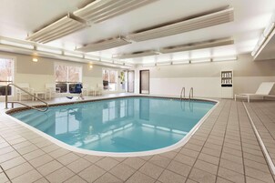 Uma piscina interior com água azul cristalina, chão em azulejos e iluminação no teto.