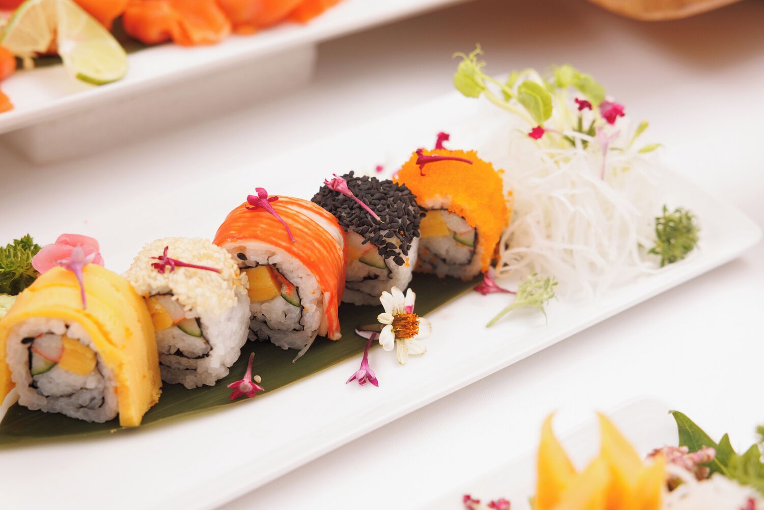 Diversos tipos de sushi em um prato branco, com acompanhamentos.