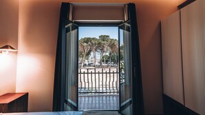 Quarto de hotel com uma grande porta de correr de vidro que dá para uma varanda com vista para árvores e carros estacionados.