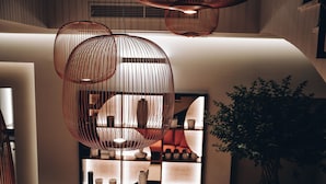 Interior moderno com ampla sala de estar integrada, luminária central com design trançado, sofá e uma coleção de objetos decorativos em prateleiras.