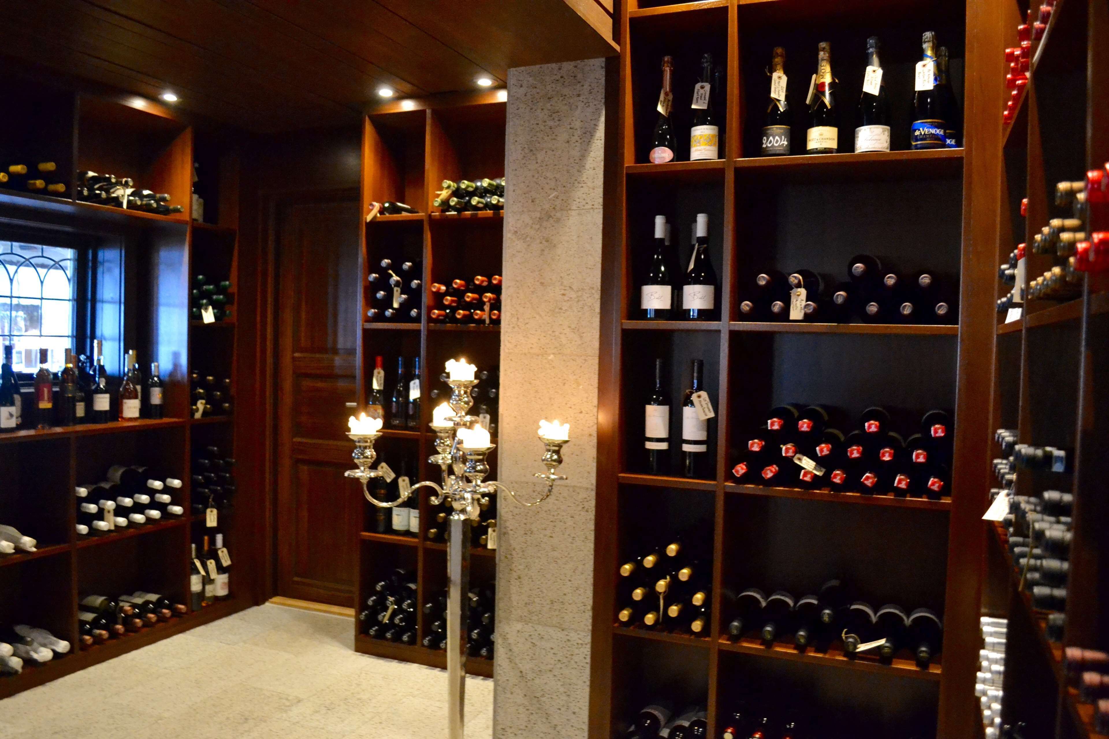Adega com prateleiras repletas de garrafas de vinho e um candelabro.