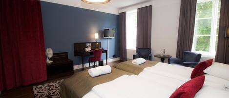 Quarto de hotel com uma cama grande, uma escrivaninha com cadeira, uma televisão e uma pequena mesa.