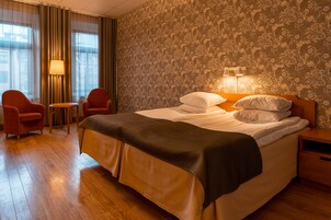 Quarto de hotel com cama, duas cadeiras, uma mesinha e um criado-mudo.