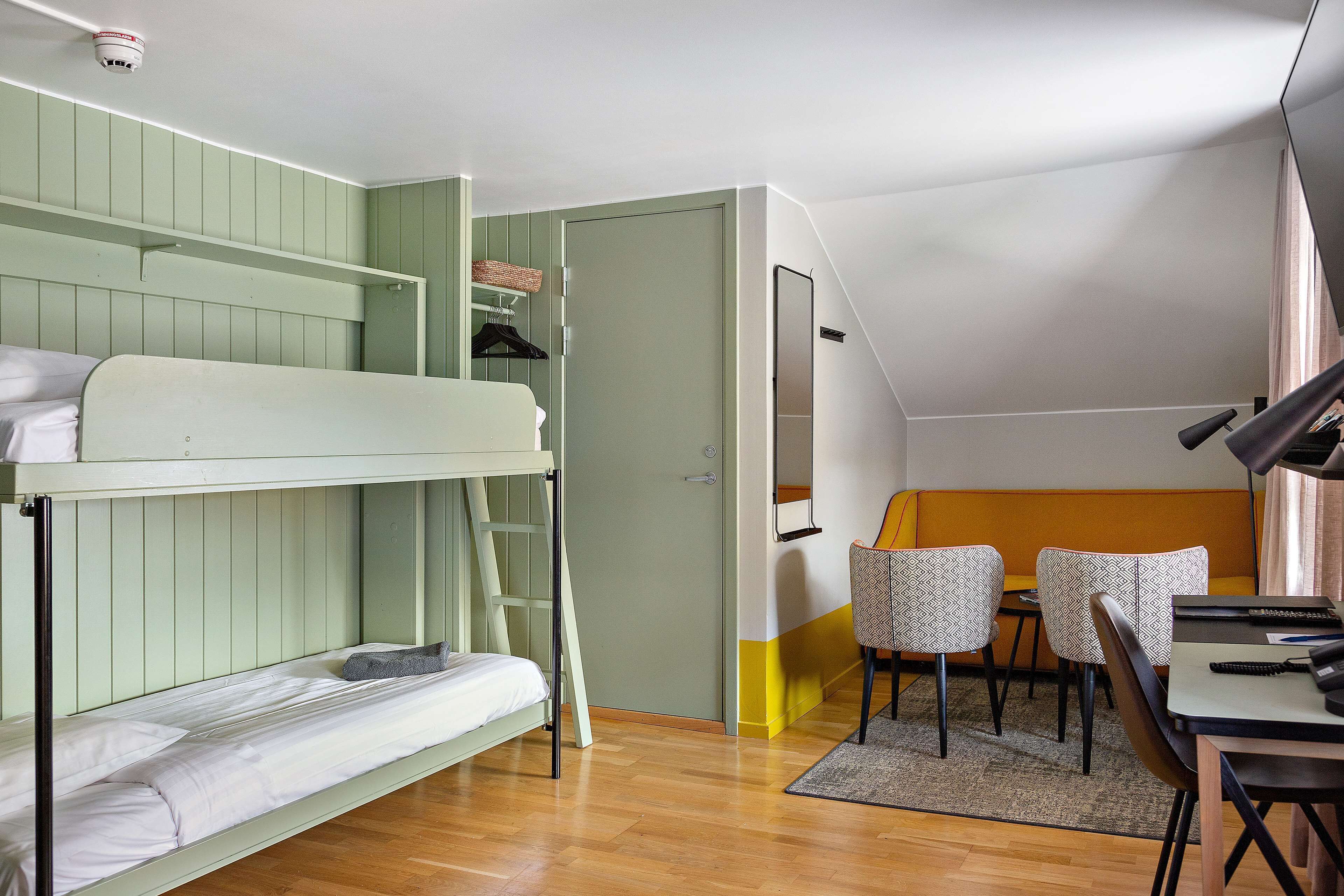 Quarto estilo dormitório com beliches, escrivaninha e cadeira.