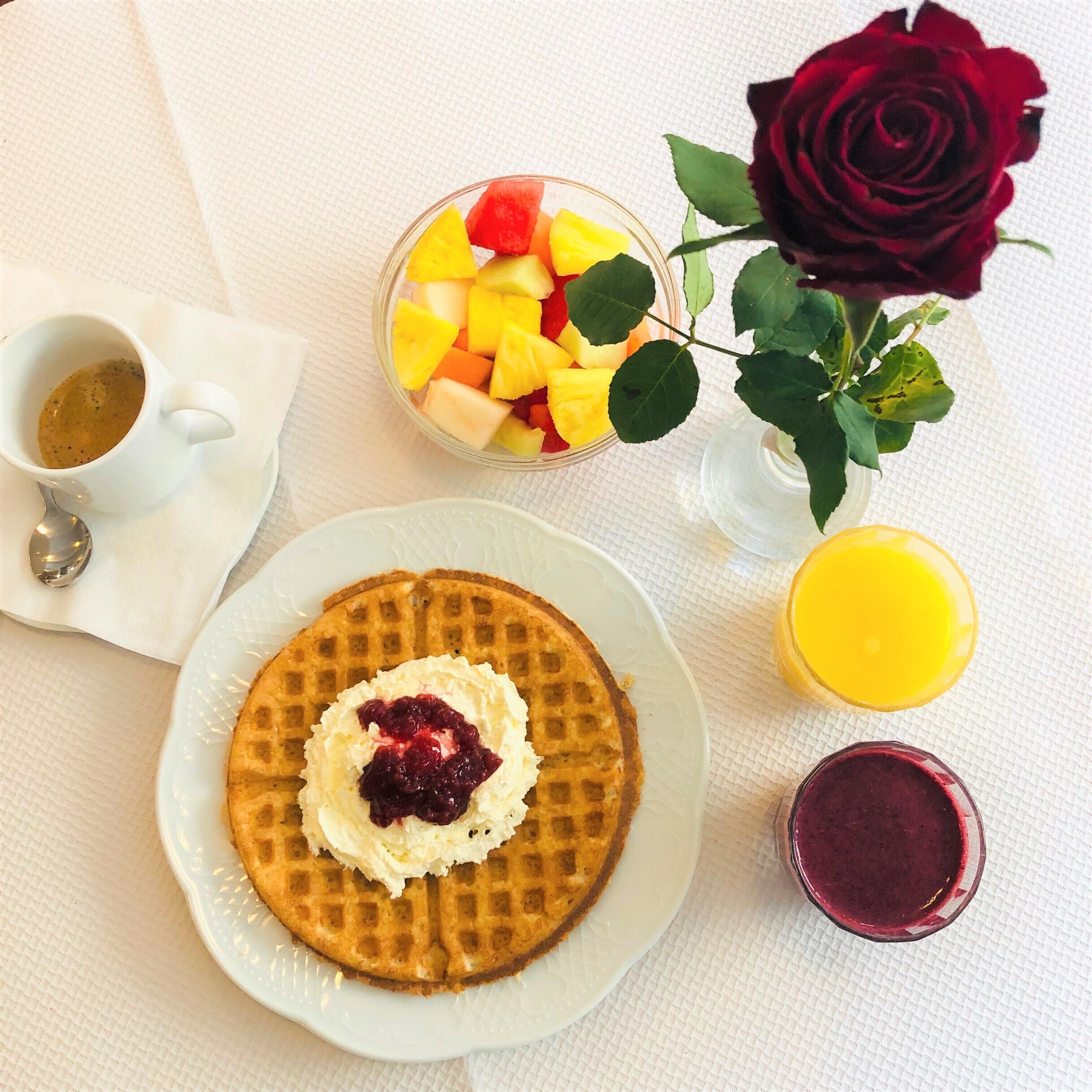 Mesa de café da manhã com waffles, frutas, café e uma rosa.
