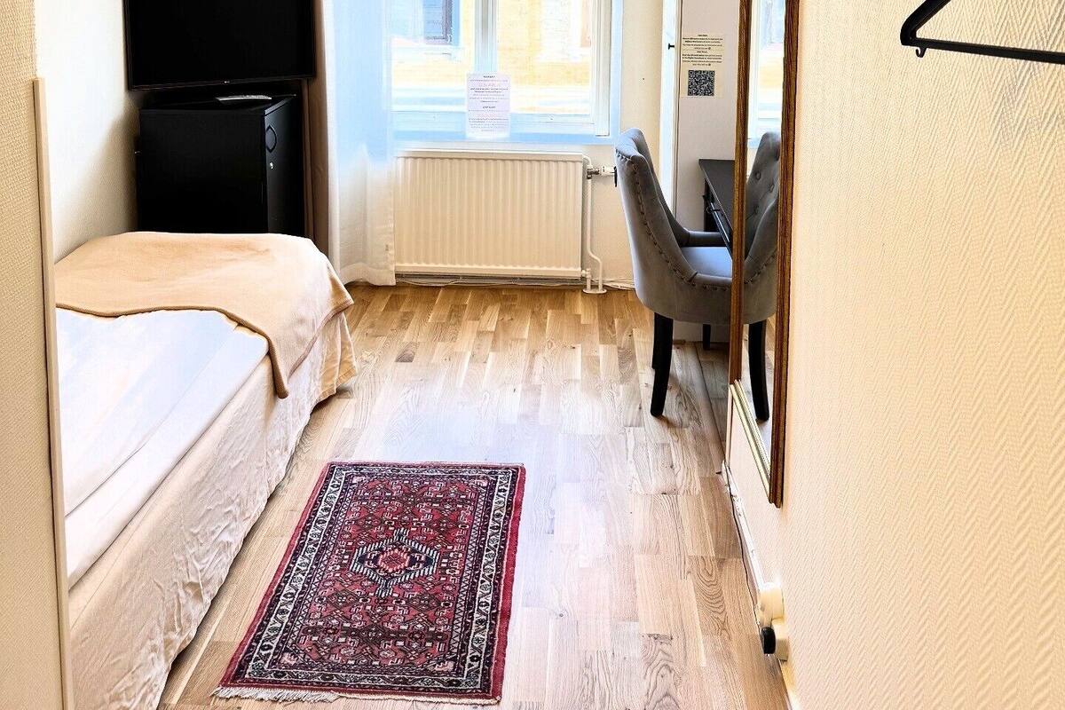 Quarto de hotel pequeno com uma cama, escrivaninha, cadeira, televisão e radiador.
