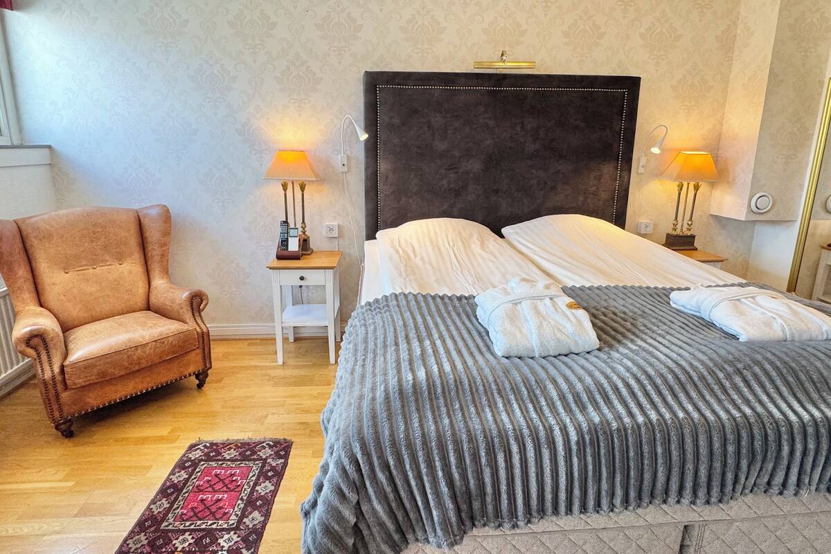 Um quarto com cama, cadeira, mesa de cabeceira e abajur.