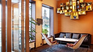 Quarto de hotel moderno com uma janela grande, um sofá, duas cadeiras, uma mesa e um painel de decoração na parede.