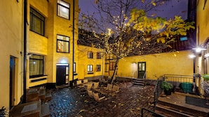 Um pátio com área de estar externa, uma árvore com luzes e um edifício com paredes amarelas.