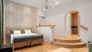 Quarto com cama, mesa de madeira, uma cadeira e escada que dá para um mezanino.