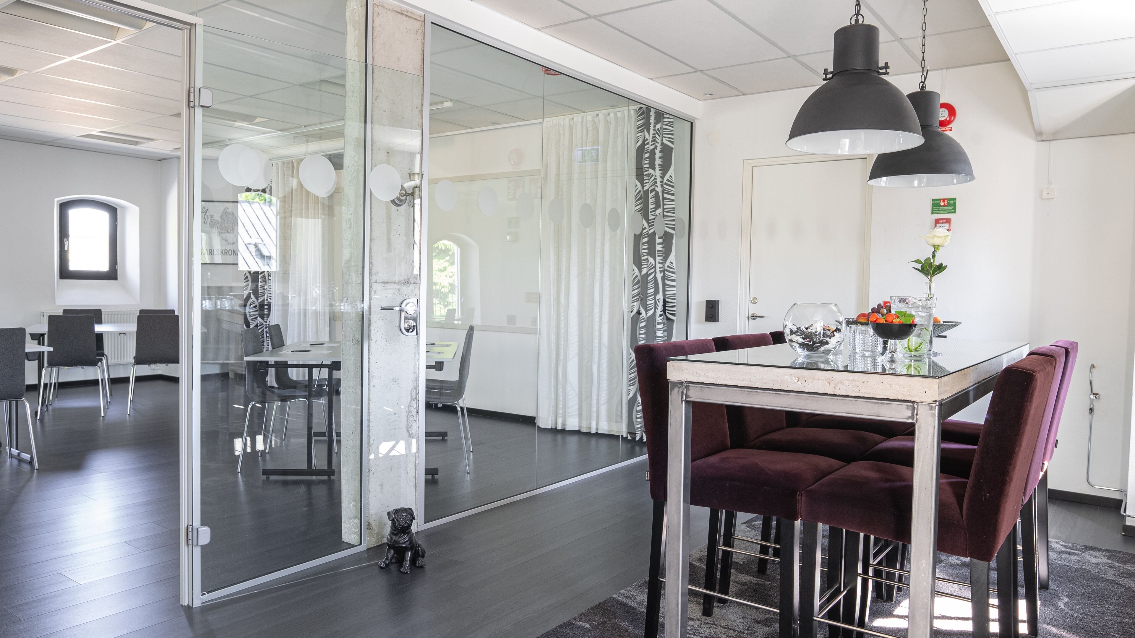 Uma área de refeições moderna com divisória de vidro, uma mesa com cadeiras e uma luminária pendente.