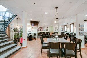 Um restaurante espaçoso com área de refeições central, uma escadaria à esquerda e piso ladrilhado.
