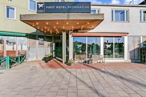 A entrada do Hotel First Brommaplan, com galeria coberta e área de estar externa.