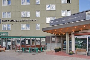Um hotel com uma placa indicando "First Hotel Brommaplan" e uma padaria chamada "Eget Bageri" no andar térreo.