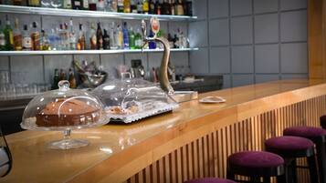 Uma área de bar com balcão de madeira, banquetas e uma seleção de garrafas e copos em prateleiras.